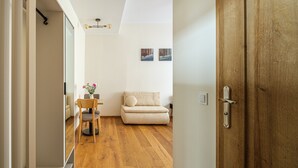 A hallway with a wooden floor, a beige sofa, a chair, and a table with a vase of flowers.