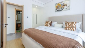 Quarto moderno com uma cama grande, um guarda-roupa e um banheiro visível por uma porta aberta.