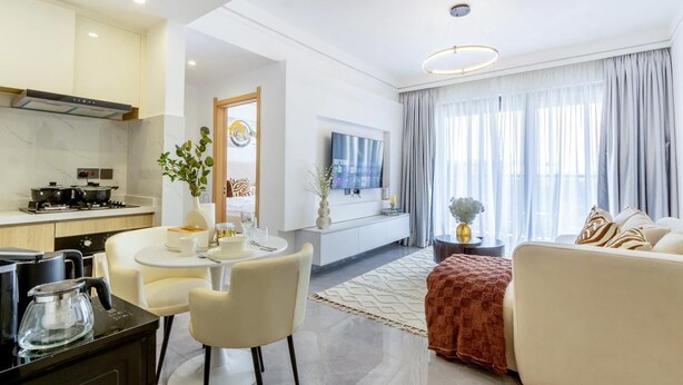 Uma sala de estar moderna com sofá, mesa de jantar com cadeiras, área de cozinha com fogão e televisão fixada na parede.