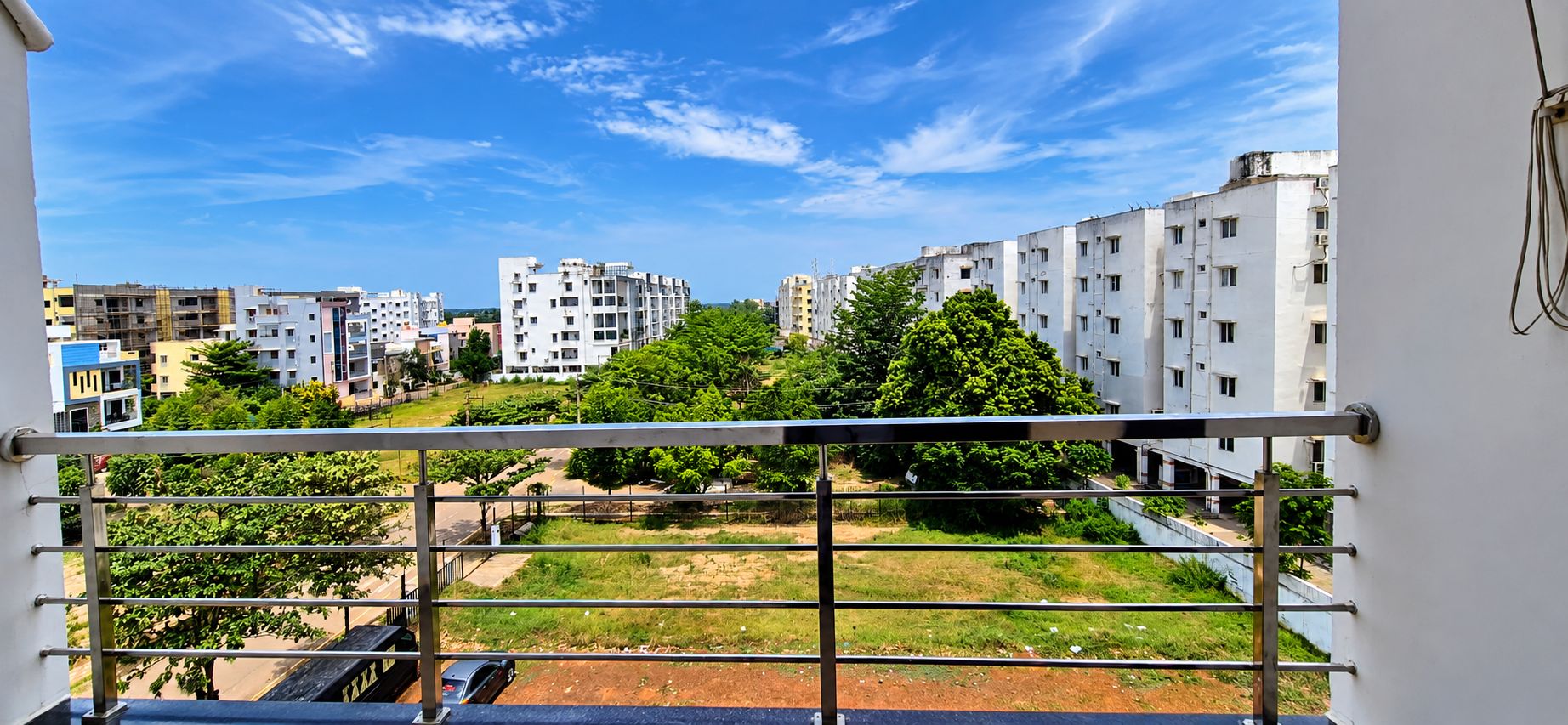Varanda com guarda-corpo de metal, vista para área residencial com prédios altos e vegetação.