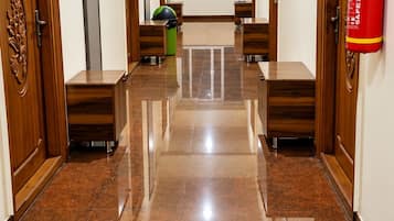 Um corredor com piso de azulejos polidos, portas de madeira e um extintor de incêndio fixado na parede.