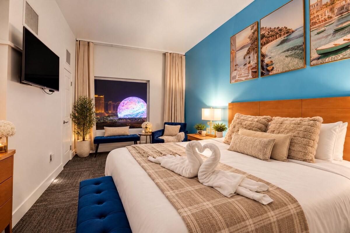 Quarto de hotel com cama grande, televisão de tela plana, vista para a cidade e parede azul decorativa.