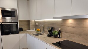 Uma cozinha moderna com armários brancos, forno de aço inoxidável, micro-ondas embutido, pia, cafeteira, um vaso de planta e uma garrafa de vinho.
