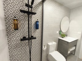 Casa de banho com parede estampada, sanita, lavatório com espelho e zona de duche com chuveiro.