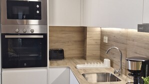 Uma cozinha moderna com armários brancos, forno embutido, torradeira, pia e cafeteira.