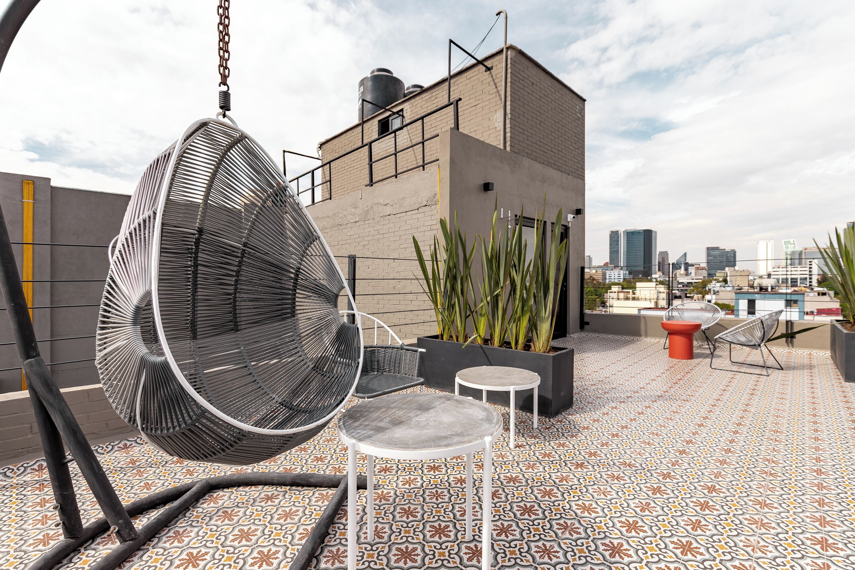 Terraço no telhado com uma cadeira suspensa, uma pequena mesa, plantas em vasos e piso estampado.