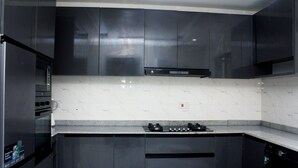 Cozinha moderna com armários escuros, geladeira de aço inoxidável, fogão a gás e lava-louças.