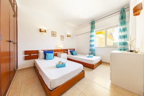 Quarto de hotel com duas camas, uma escrivaninha e uma janela com cortinas.
