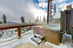 Uma banheira de hidromassagem com escadas que levam até ela, cercada por árvores cobertas de neve e um deck de madeira.