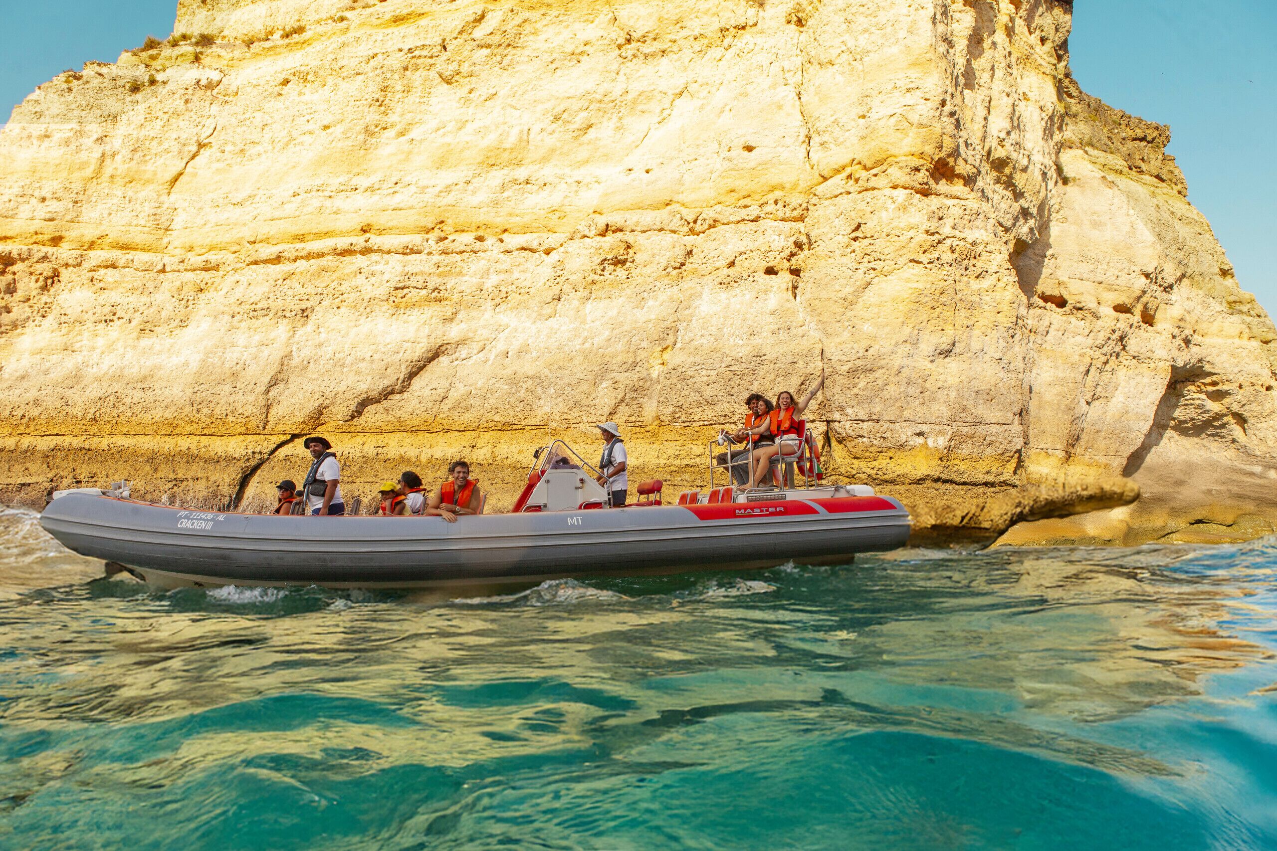 Um barco com passageiros próximo a um penhasco rochoso.
