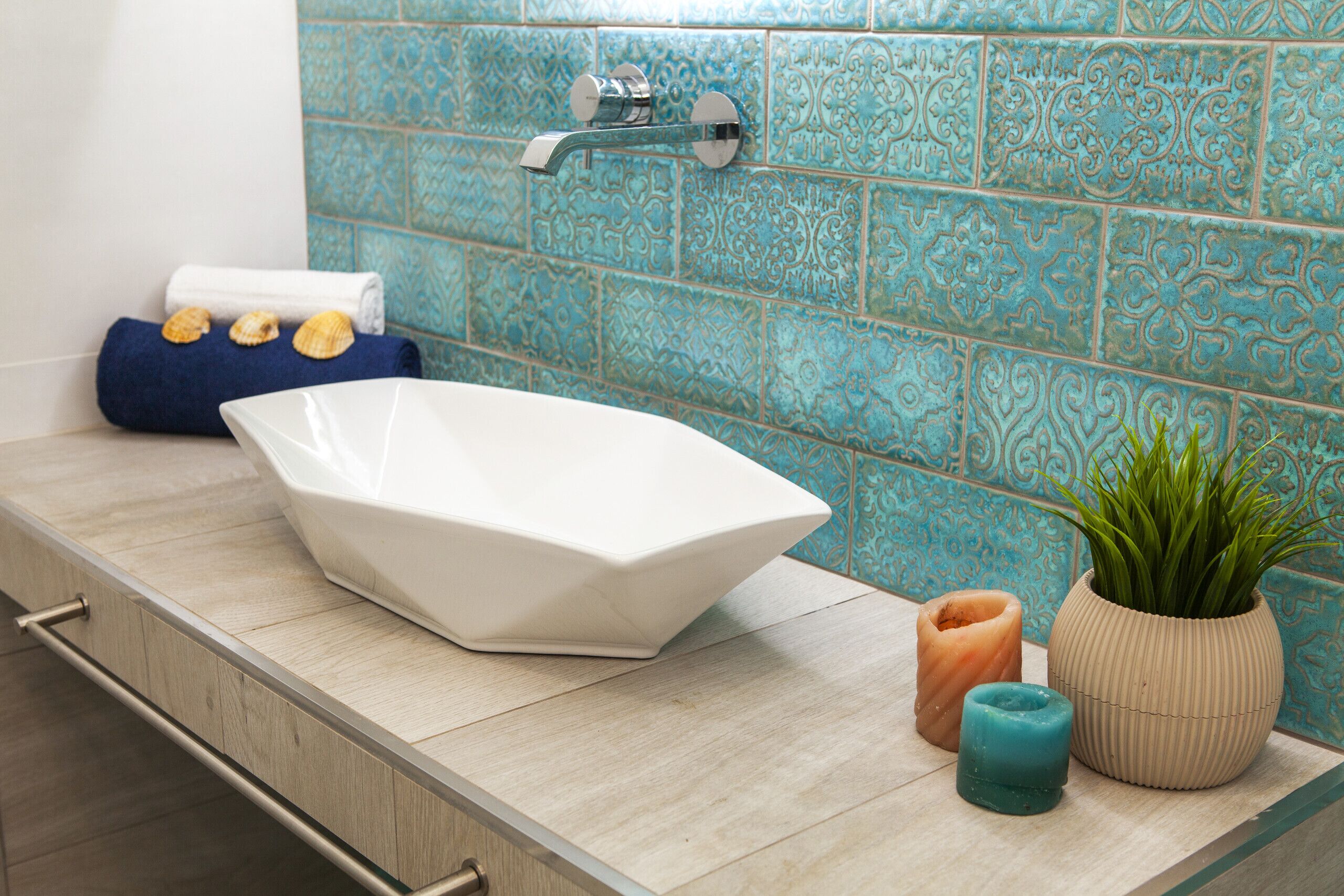 Casa de banho com lavatório suspenso branco, toalha azul, planta em vaso e uma vela decorativa.