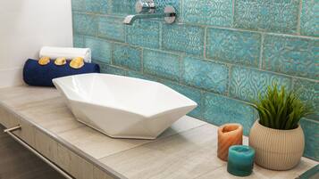 Casa de banho com lavatório suspenso branco, toalha azul, planta em vaso e uma vela decorativa.