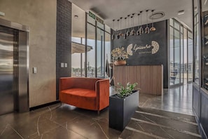 Um lobby moderno com um balcão de recepção, um sofá vermelho, uma planta em vaso e vista através de grandes janelas.