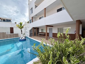 Piscina com uma palmeira, prédio com várias varandas e área de terraço.