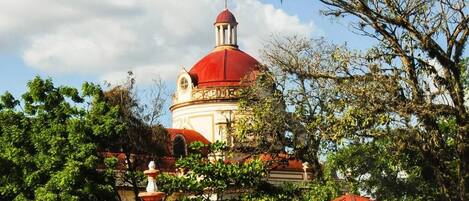 Uma igreja com cúpula vermelha e uma cruz no topo, rodeada por árvores.