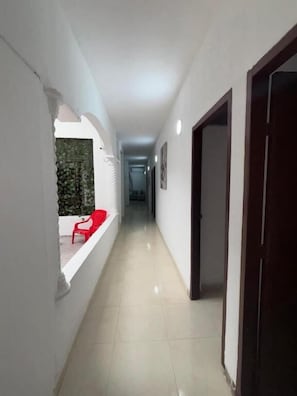 Um corredor estreito com um banco vermelho, paredes brancas e uma porta à direita.