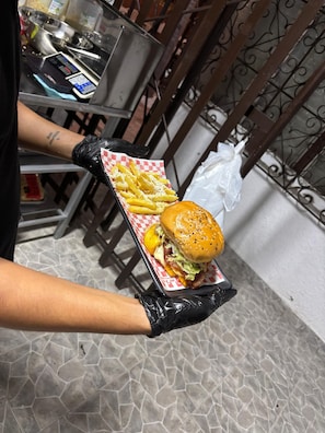Uma pessoa segurando uma bandeja com um hambúrguer e batatas fritas.