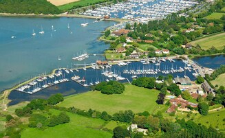 Vista aérea de uma marina com vários barcos atracados, cercada por propriedades residenciais e vegetação.