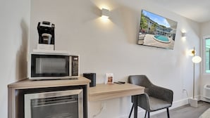 Quarto moderno com micro-ondas, máquina de café e TV exibindo vista para a piscina.
