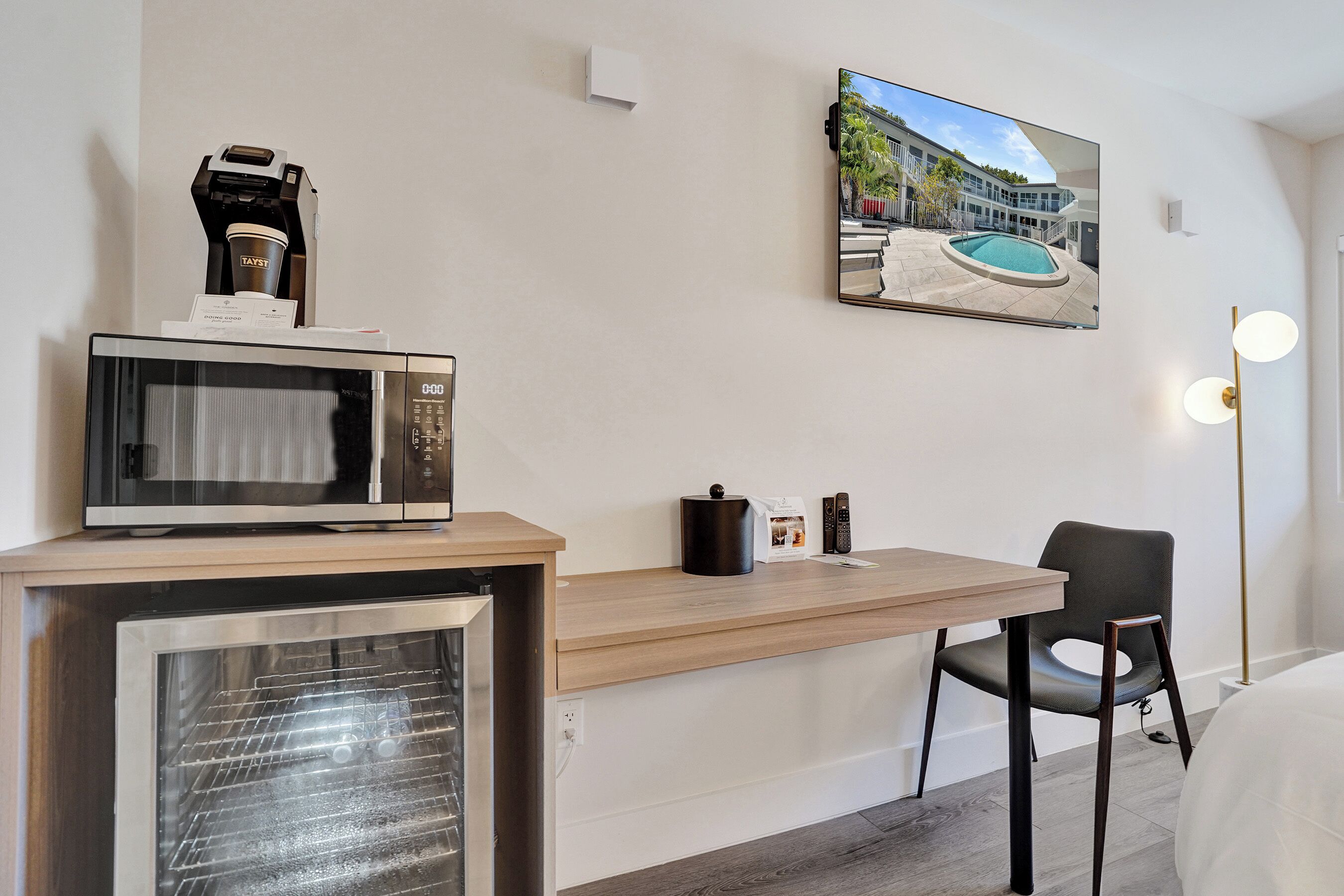 Quarto de hotel com cozinha compacta, televisão presa na parede, cama e escrivaninha com cadeira.