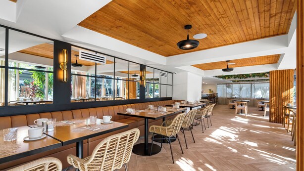 Um café moderno com teto de madeira, janelas amplas e mobiliário de vime.