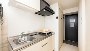 Uma cozinha compacta com uma pia de aço inoxidável, um exaustor preto e um pequeno balcão com escorredor de louça.