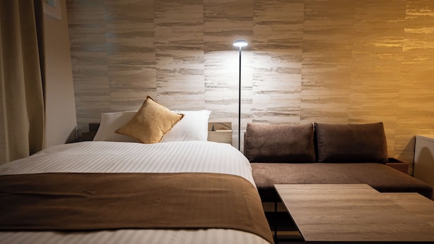 Quarto de hotel moderno com uma cama grande, uma mesinha de cabeceira, um abajur e um sofá.