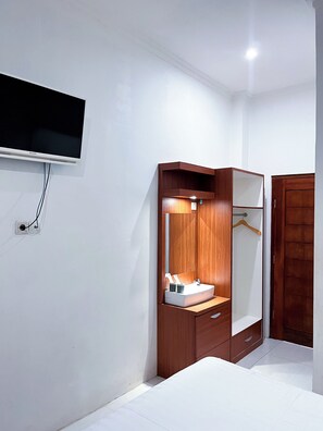 Quarto com cama, guarda-roupa, espelho, televisão presa à parede e tomada.