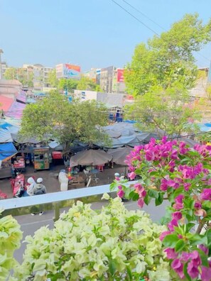 Uma área de mercado com barraquinhas e pessoas, cercada por edifícios e árvores.