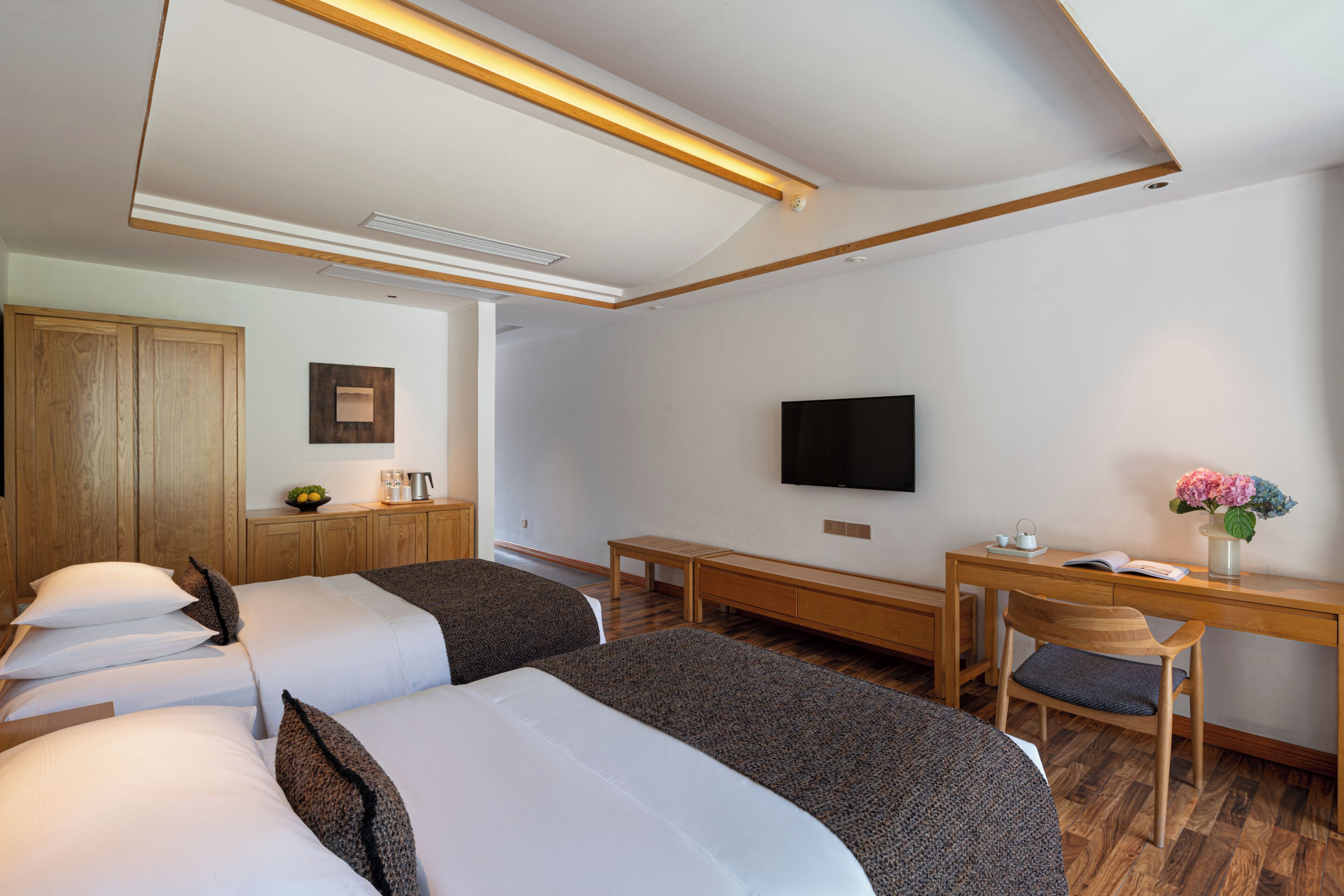 Quarto de hotel com duas camas, uma escrivaninha, televisão e guarda-roupa de madeira.