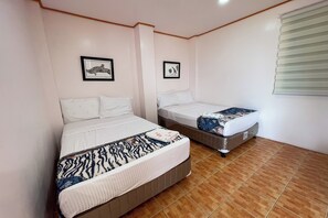 Duas camas com roupa de cama branca, um cobertor estampado e duas molduras com quadros nas paredes.