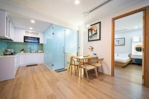 Uma cozinha compacta com eletrodomésticos modernos, um espaço de refeições com mesa e cadeiras, e um quarto com cama e escrivaninha.