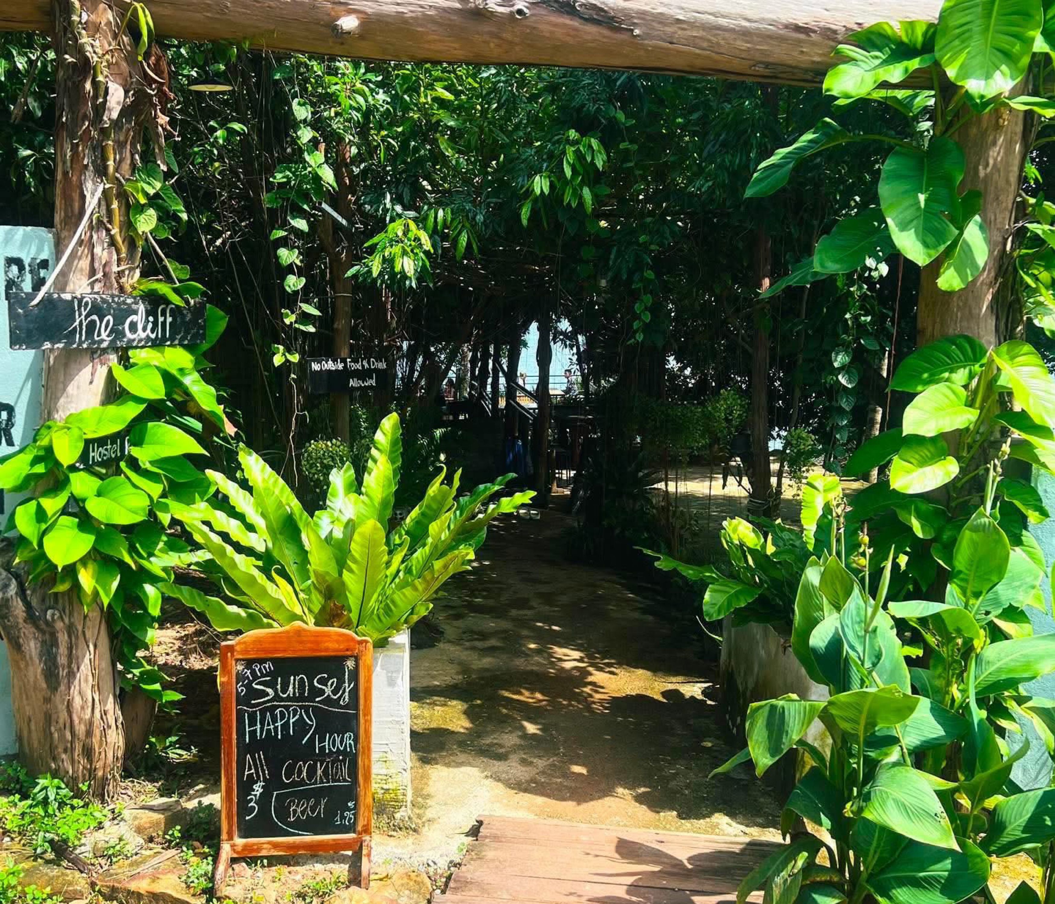 Área externa de café com quadro negro anunciando promoções de happy hour, com coquetéis e cerveja.
