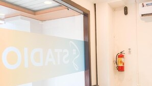 Uma área de recepção com um sofá de couro preto, um painel de vidro com um logotipo e um extintor de incêndio na parede.