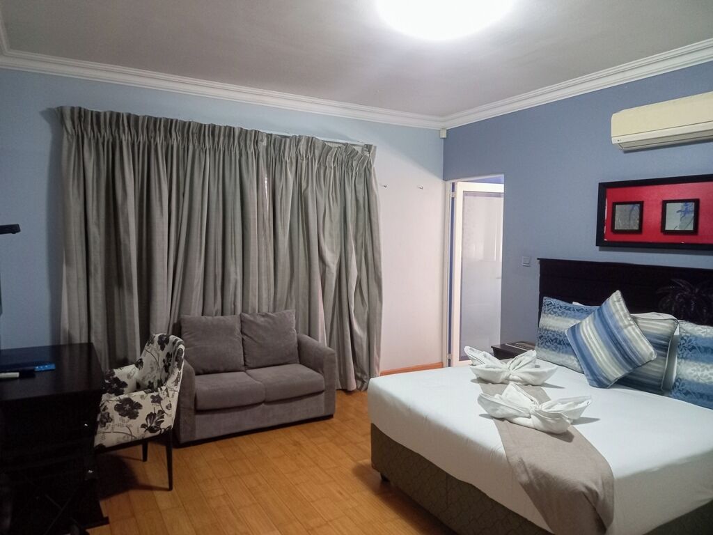 Um quarto com cama, sofá, cadeira, escrivaninha e cortinas.