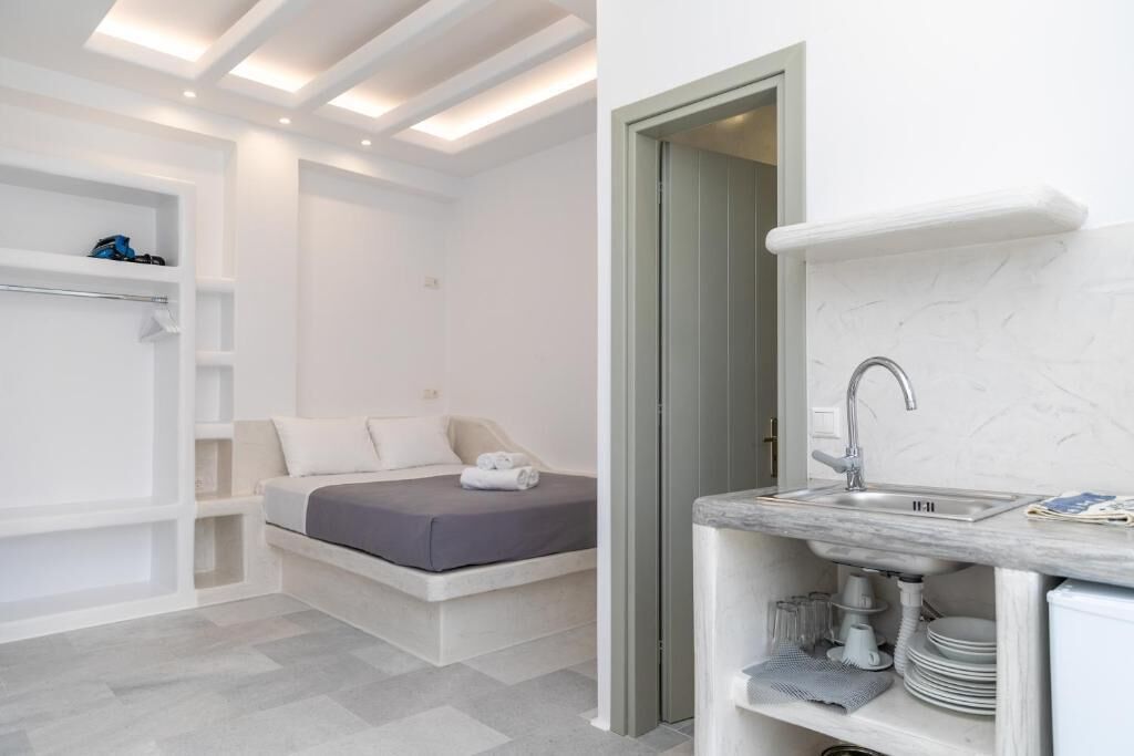 Quarto moderno com cama, estantes embutidas, banheiro com pia e espelho, e closet espaçoso.