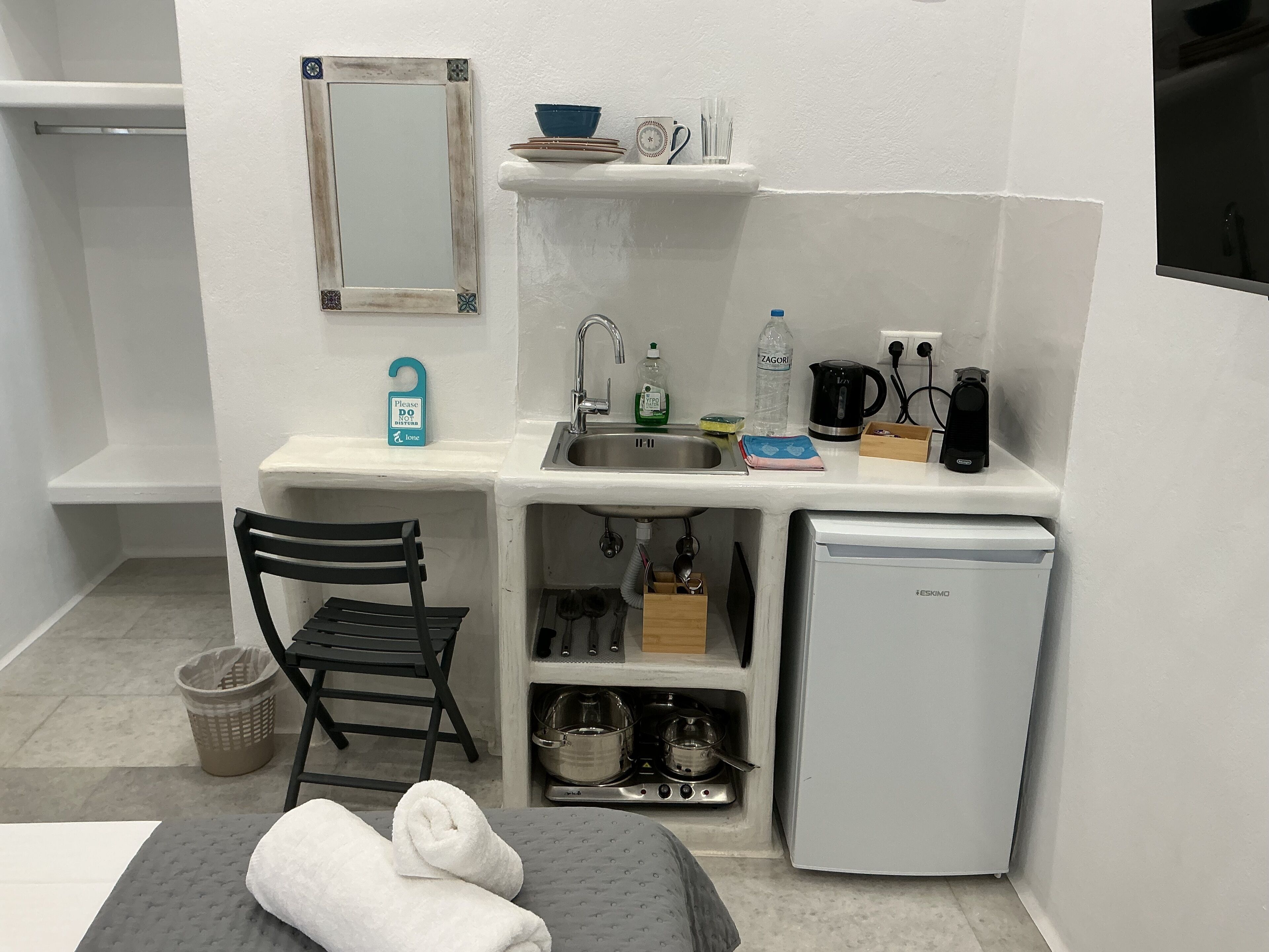 Uma kitchenette compacta com pia, um pequeno frigorífico, fogão e uma cadeira.