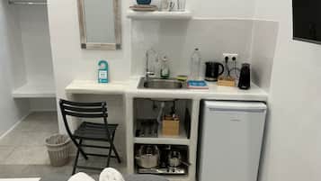Uma kitchenette compacta com pia, um pequeno frigorífico, fogão e uma cadeira.