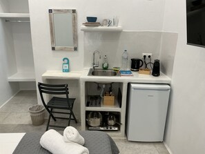Uma kitchenette compacta com pia, um pequeno frigorífico, fogão e uma cadeira.