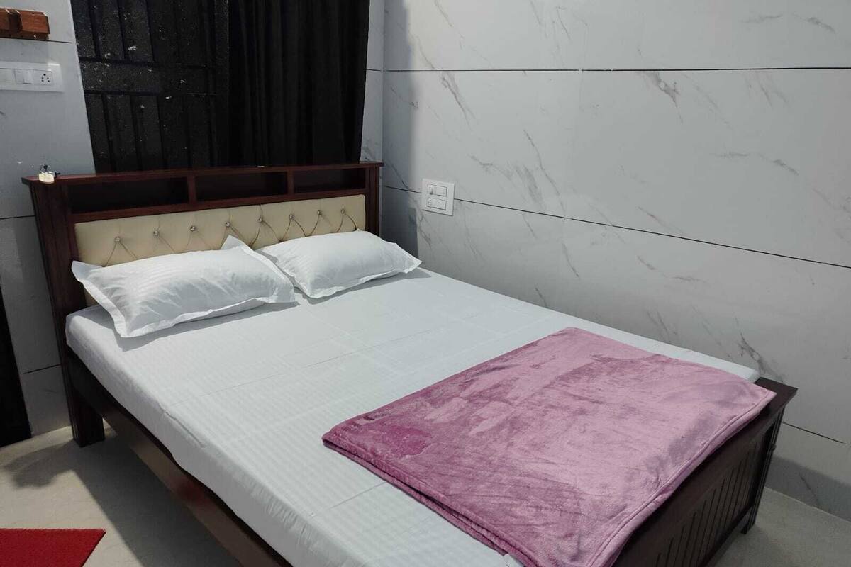 Uma cama de solteiro com cabeceira de madeira, roupa de cama branca e manta rosa.