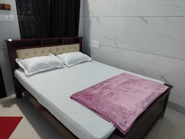 Uma cama de solteiro com cabeceira de madeira, roupa de cama branca e manta rosa.