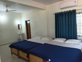 Quarto com duas camas, ventilador de teto, ar condicionado, janela com cortinas e uma pia pequena.