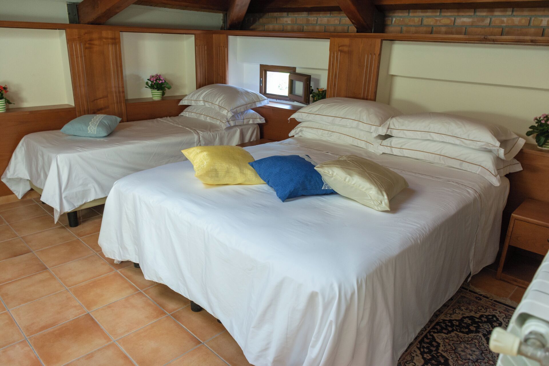 Duas camas de solteiro com roupa de cama branca, um travesseiro azul e um travesseiro amarelo na cama em primeiro plano.