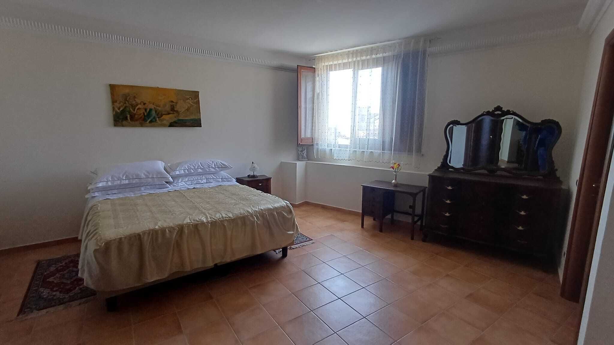 Um quarto com cama, cômoda, escrivaninha, janela com cortinas e um quadro na parede.
