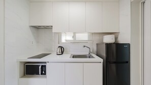 Uma cozinha moderna com armários brancos, uma pia de aço inoxidável, uma geladeira preta, uma chaleira e um micro-ondas.