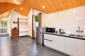 Cozinha moderna com teto de madeira, armários brancos, geladeira de aço inoxidável, micro-ondas e pia.