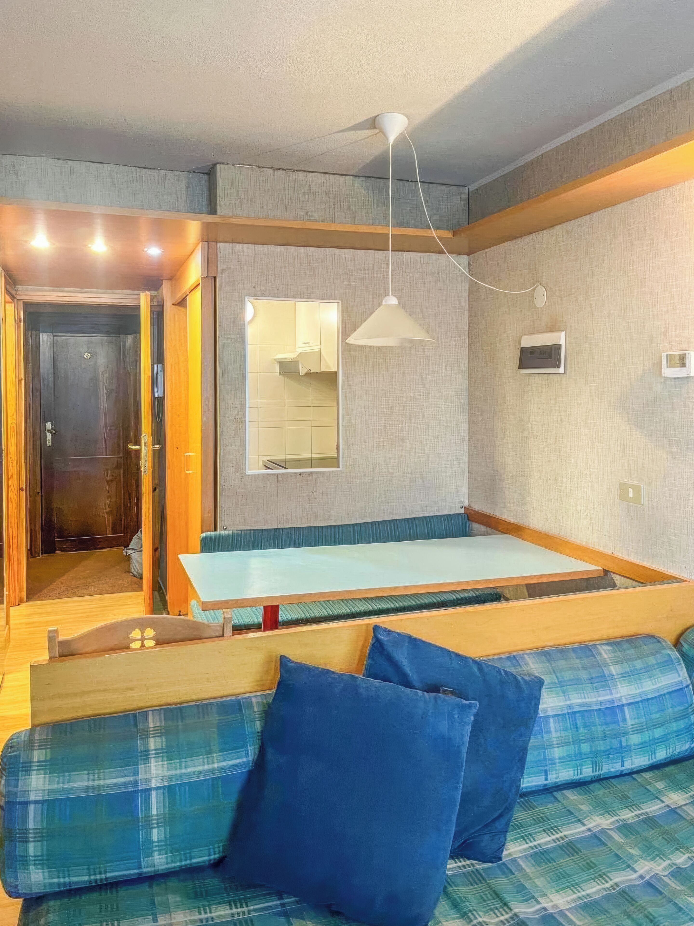 Um quarto com um banco de madeira, um sofá com almofadas azuis, um lustre pendurado e um espelho na parede.