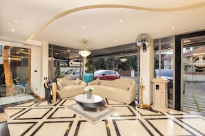 Um lobby moderno com um candelabro, sofás, uma mesa de centro e um vaso grande com flores.