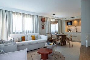 Uma sala de estar moderna com sofá, mesa de jantar e cadeiras, área de cozinha com micro-ondas e uma grande janela com cortinas.
