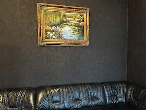 Paredes escuras com um quadro de uma cena de jardim e um sofá de couro preto.